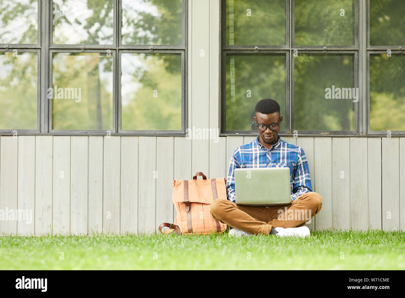 Full length portrait of smart African student using laptop outdoors ...