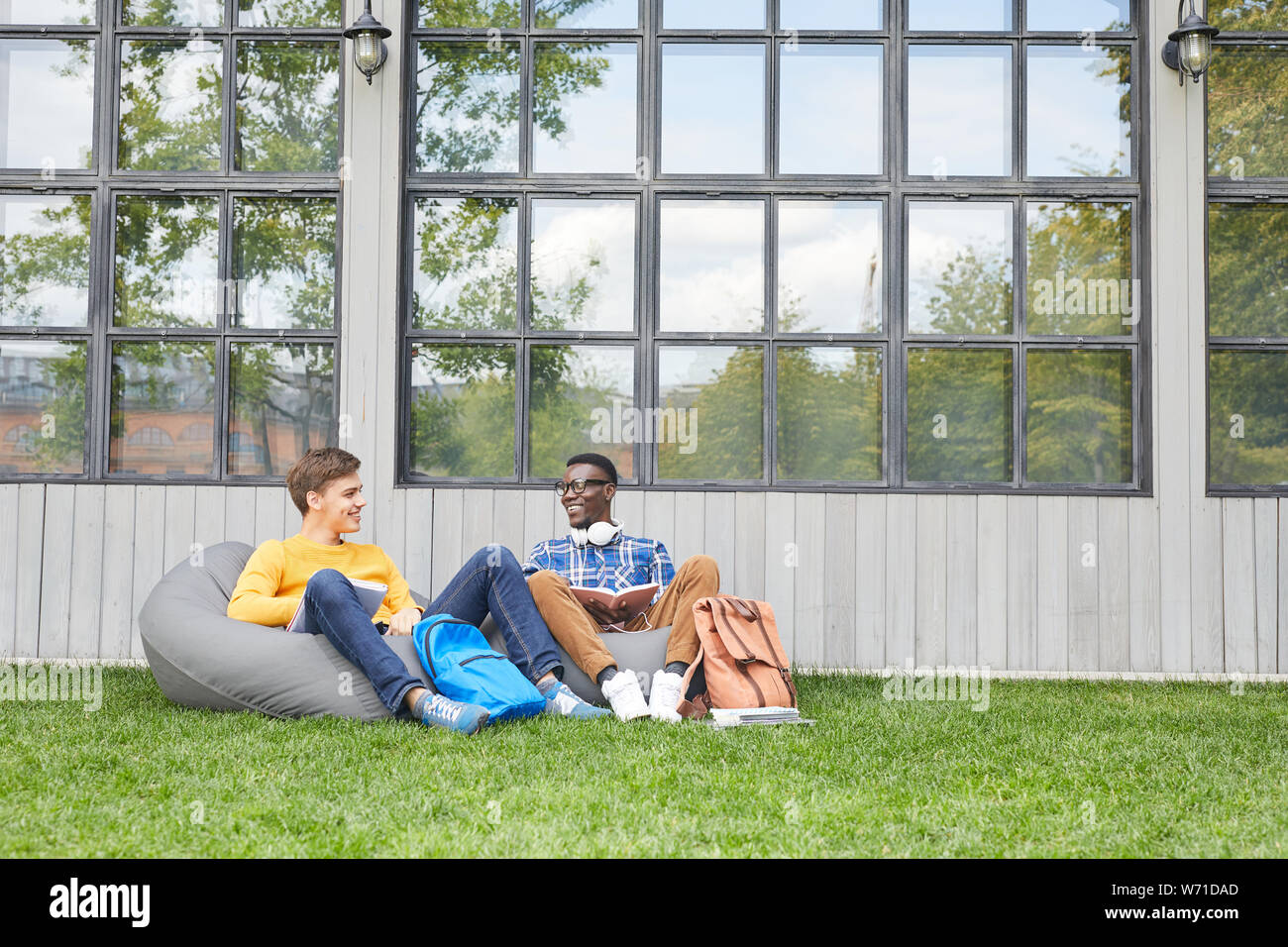 Full length portrait of two students relaxing outdoors in college ...