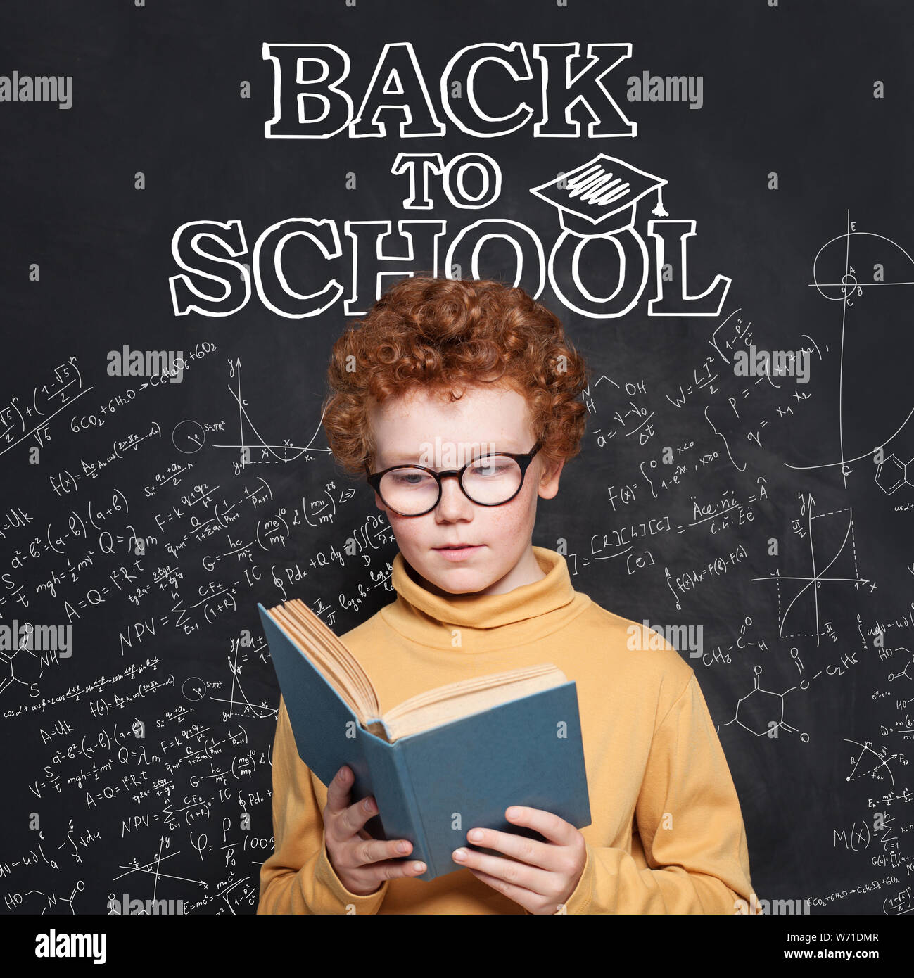 Curious child reading a book on chalkboard background. Back to school ...