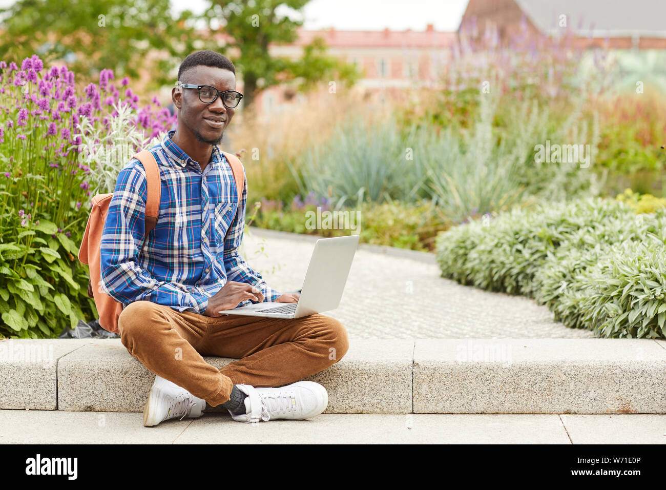 Full length portrait of African student smiling at camera while using ...