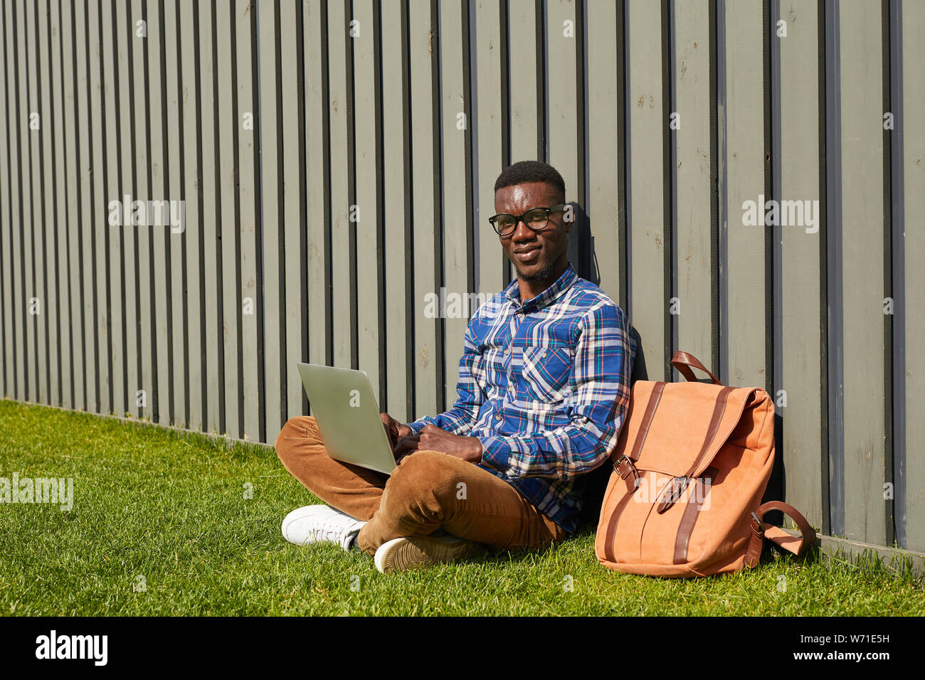 Full length portrait of African student looking at camera while using ...