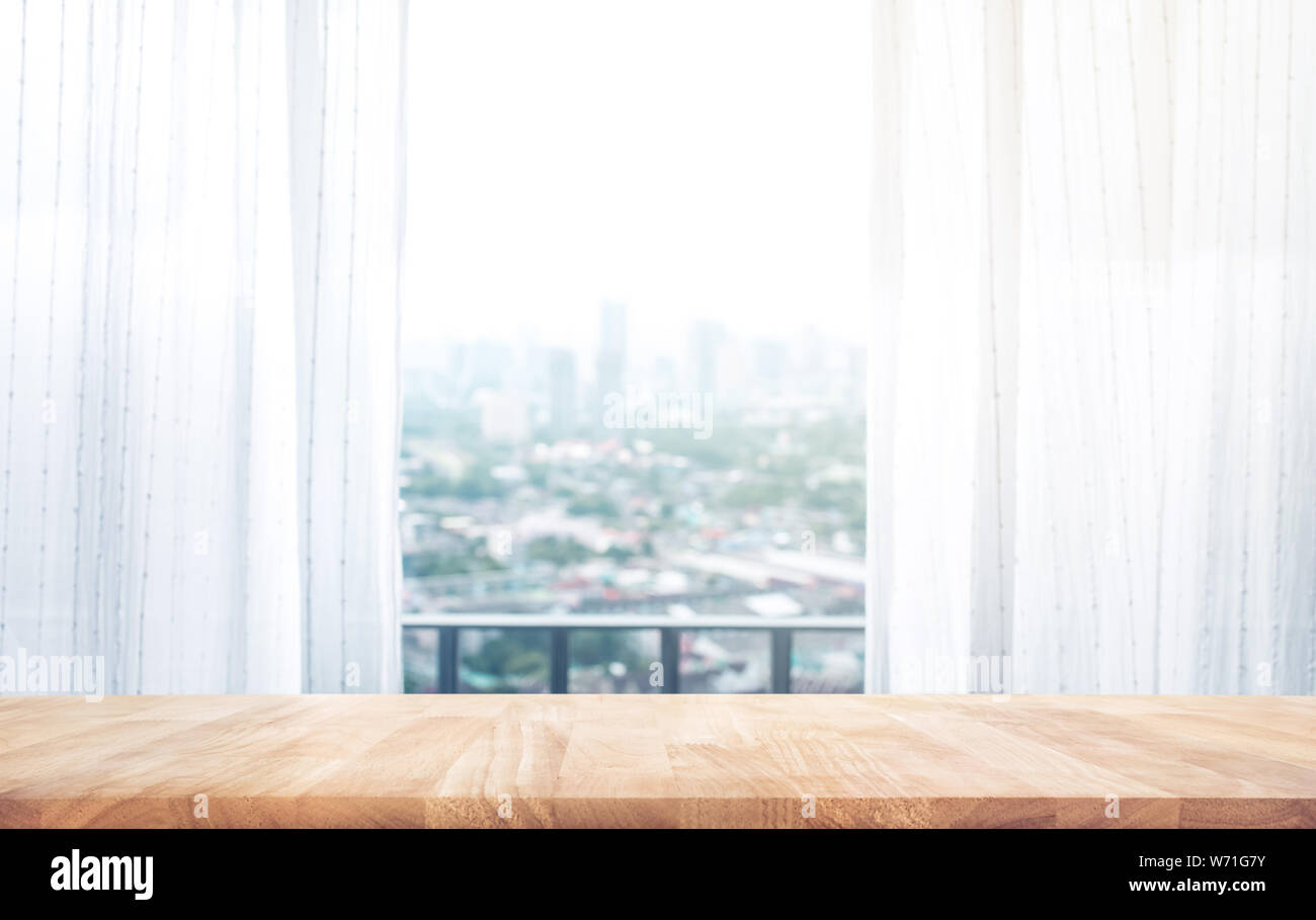 Wood table top on on blur of curtain with window city view background ...