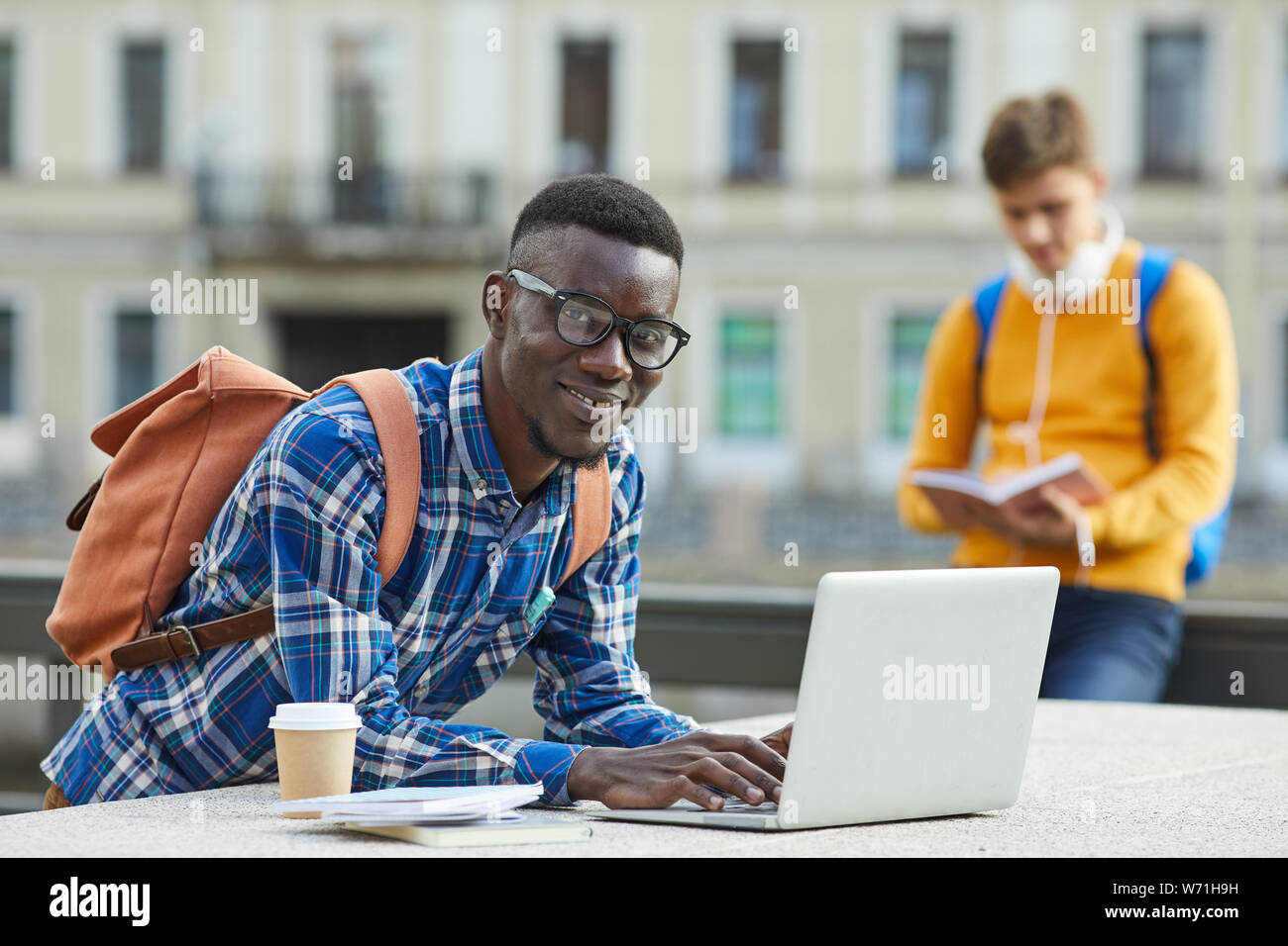 Portrait of contemporary African student using laptop outdoors in ...
