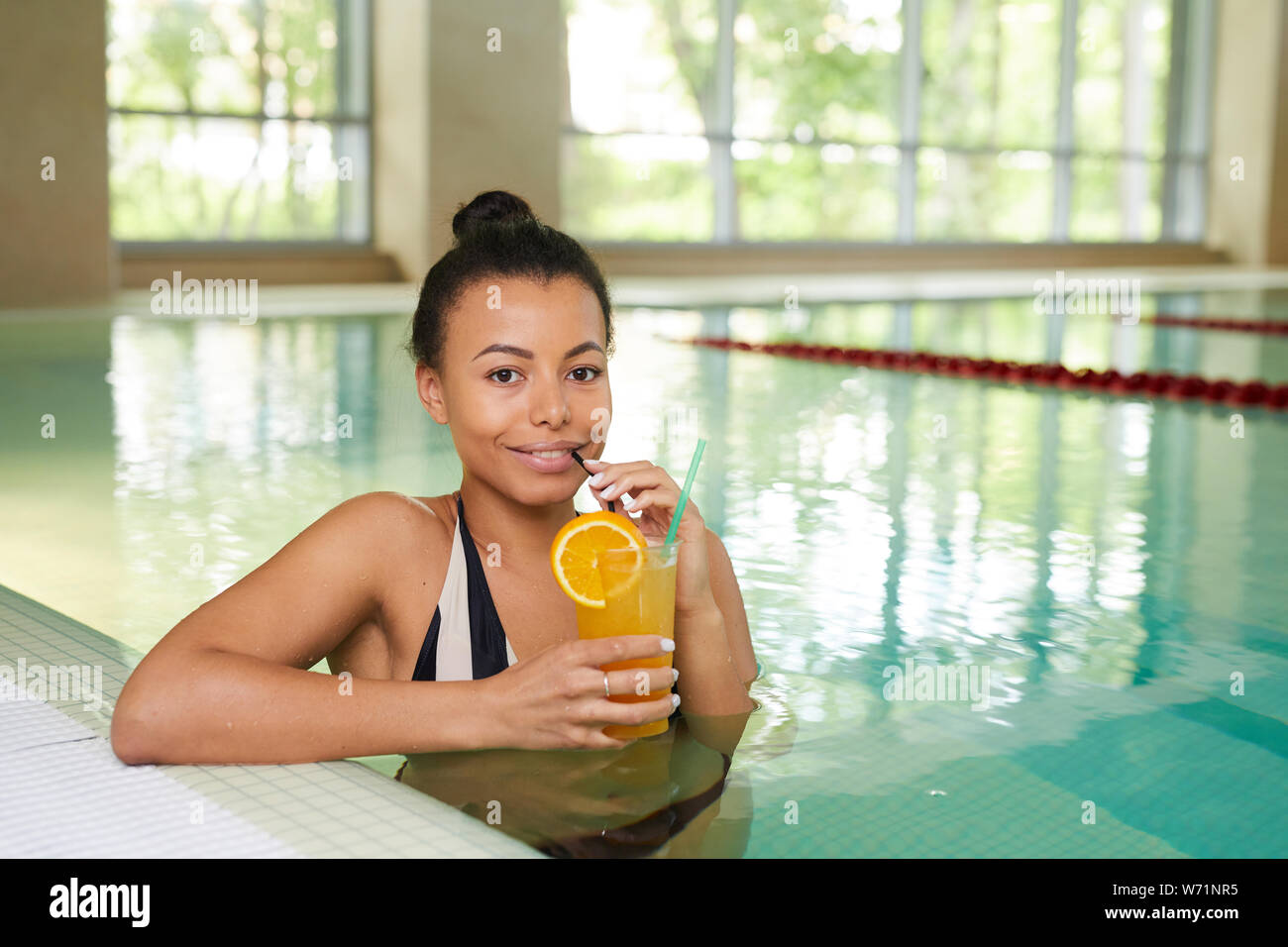 Portrait of beautiful woman drinking cocktail in swimming pool while ...