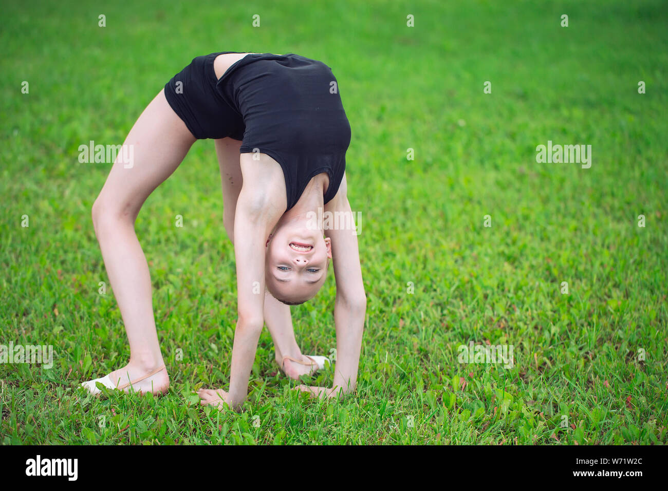 Beautiful little girl doing gymnastics on the grass on a sunny day ...