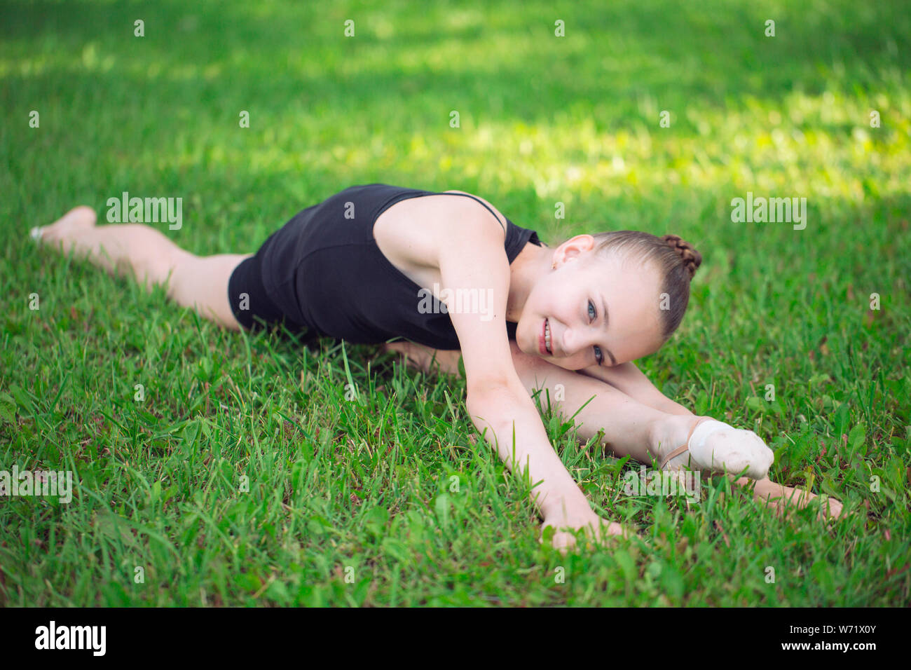 Beautiful little girl doing gymnastics on the grass on a sunny day ...