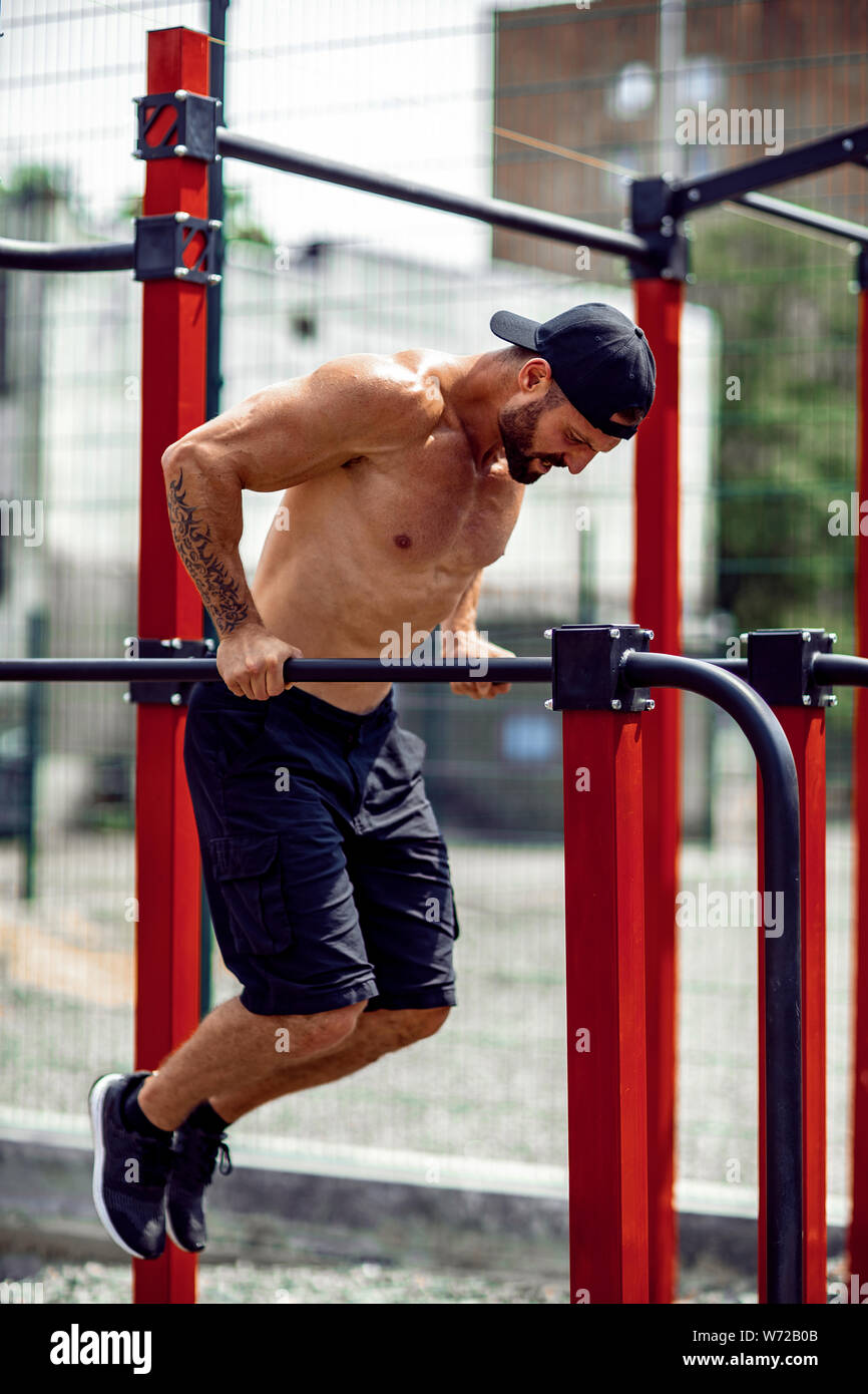 Strong muscular man doing push-ups on uneven bars in outdoor street gym ...