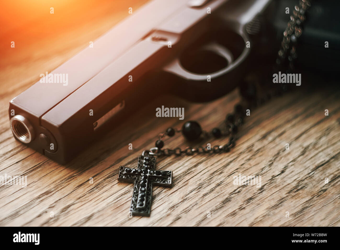 On the old wooden surface is a gun and a rosary with a black cross on a ...
