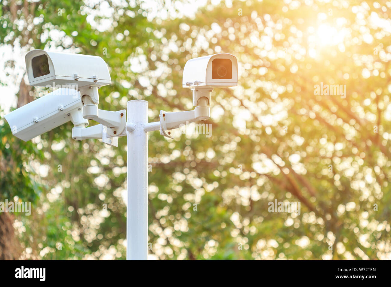 White security CCTV camera installed in the park at public area on blur ...
