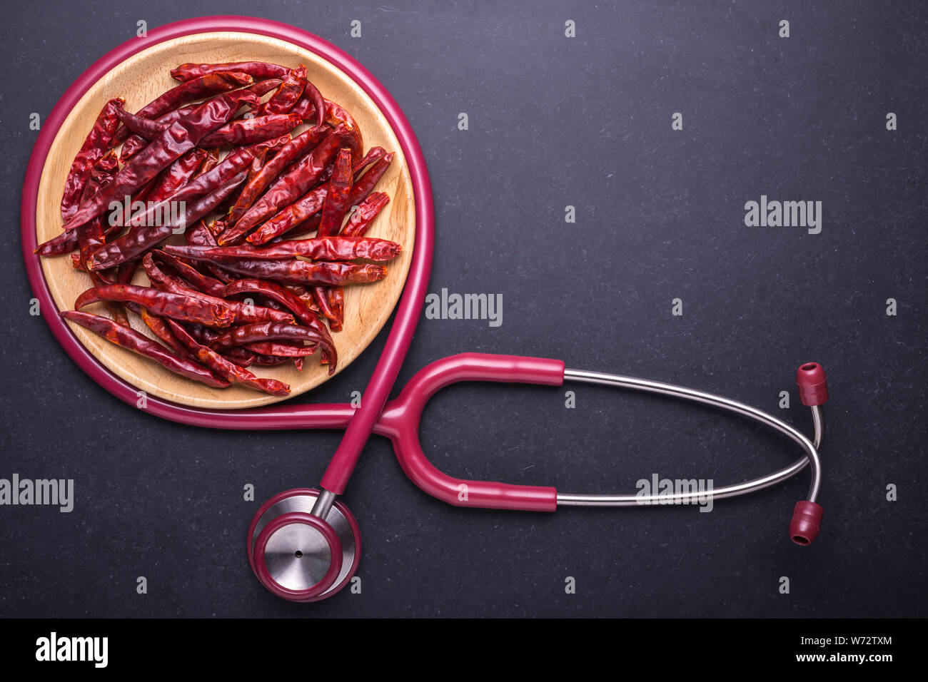 Top view dry red hot chilli and doctor stethoscope on black stone board ...