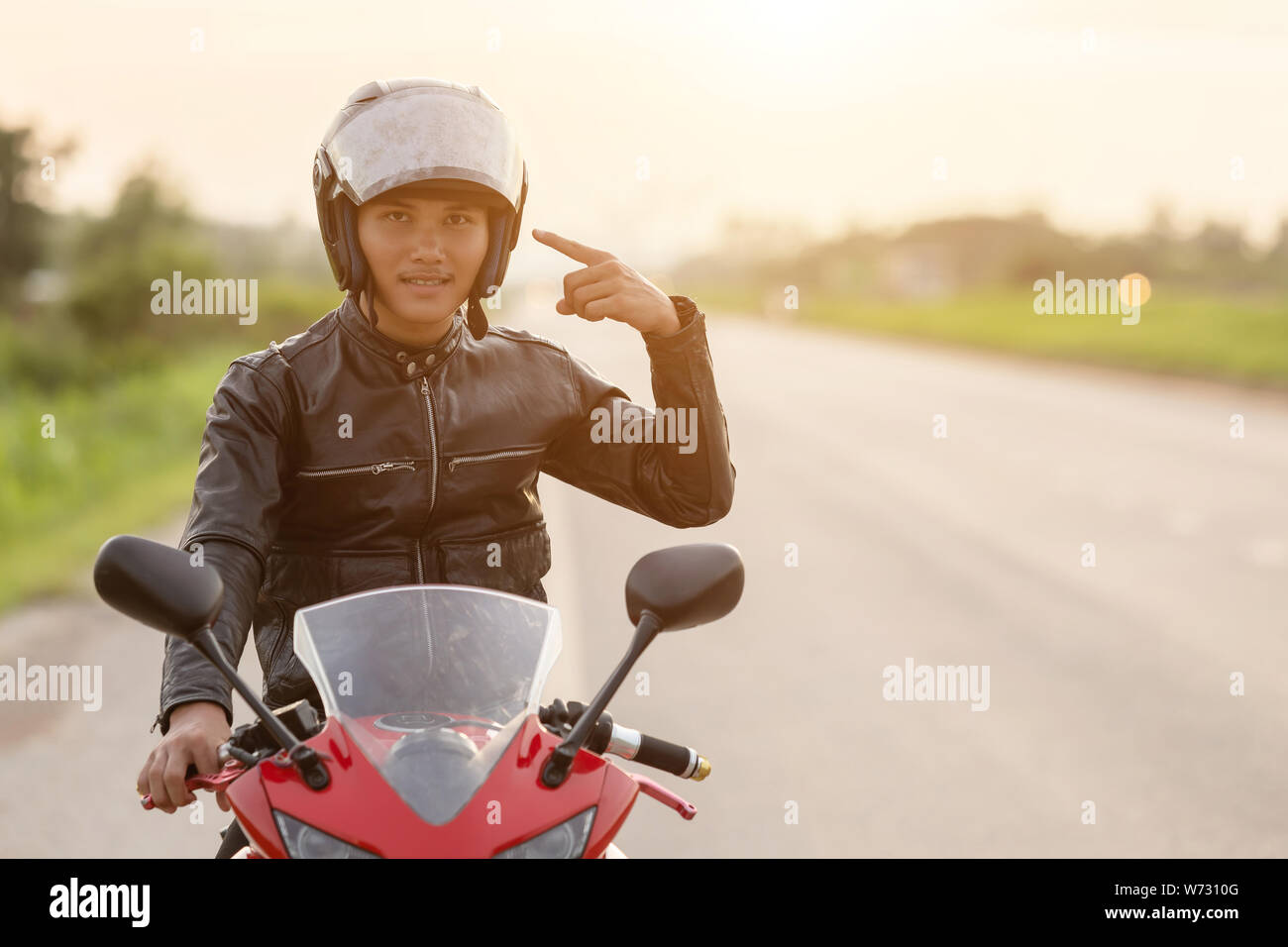Handsome motorcyclist point the finger to his helmet. Wear the helmet ...
