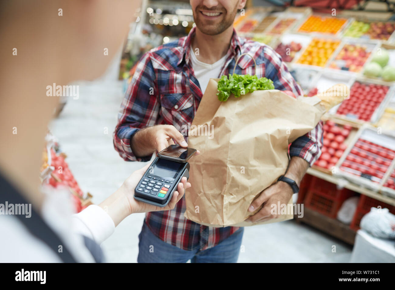 Mid section portrait of smiling man paying via smartphone at farmers ...
