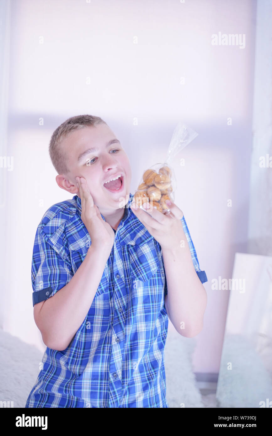 cute hungry teenager boy with fresh small bake sweets on white room ...