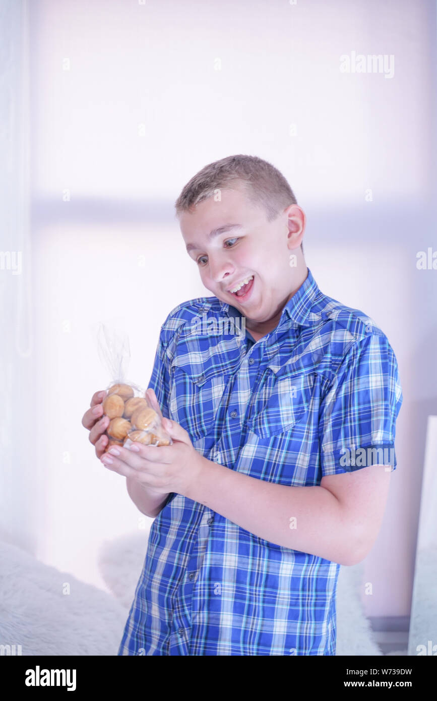 cute hungry teenager boy with fresh small bake sweets on white room ...