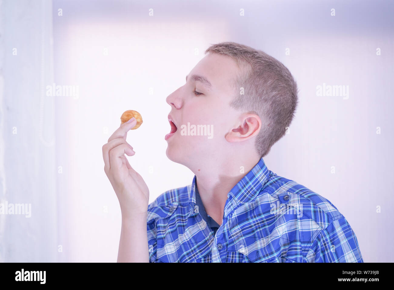 cute hungry teenager boy with fresh small bake sweets on white room ...