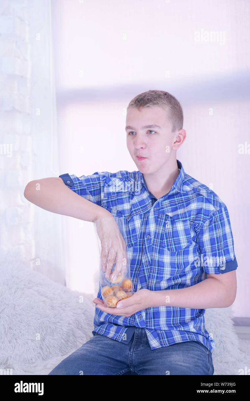 cute hungry teenager boy with fresh small bake sweets on white room ...