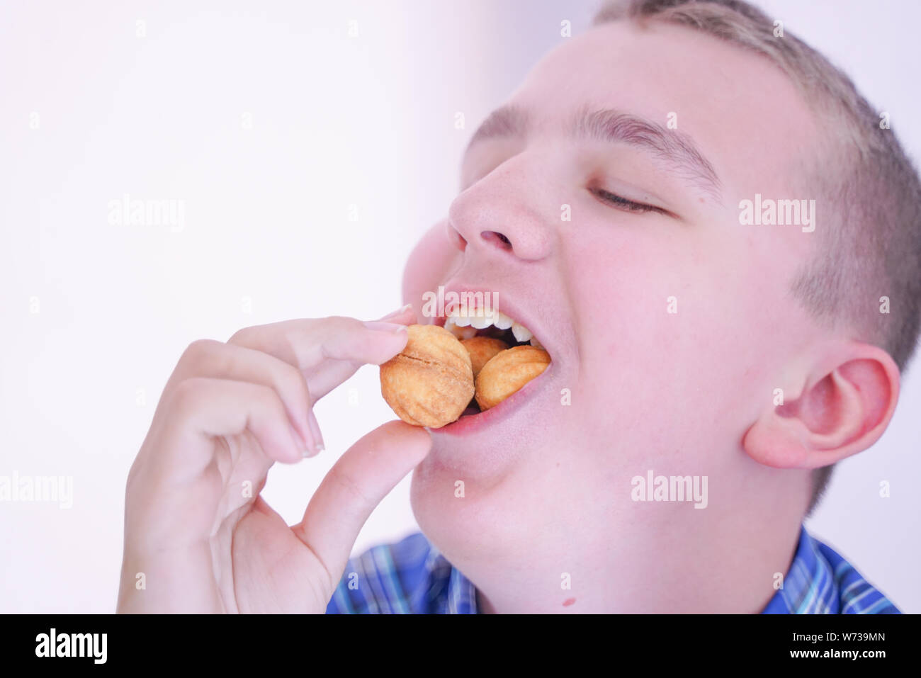cute hungry teenager boy with fresh small bake sweets on white room ...
