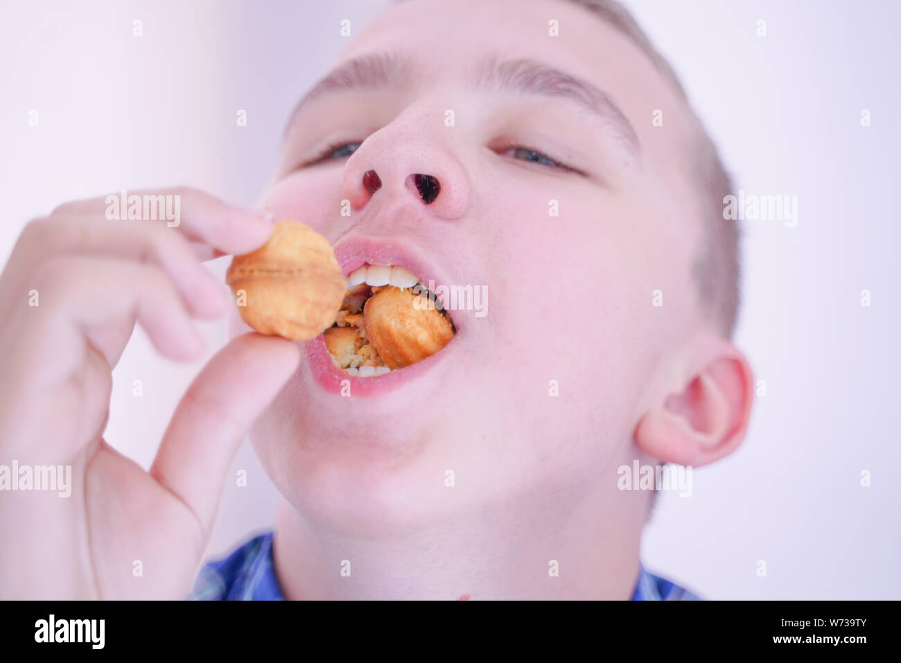 cute hungry teenager boy with fresh small bake sweets on white room ...