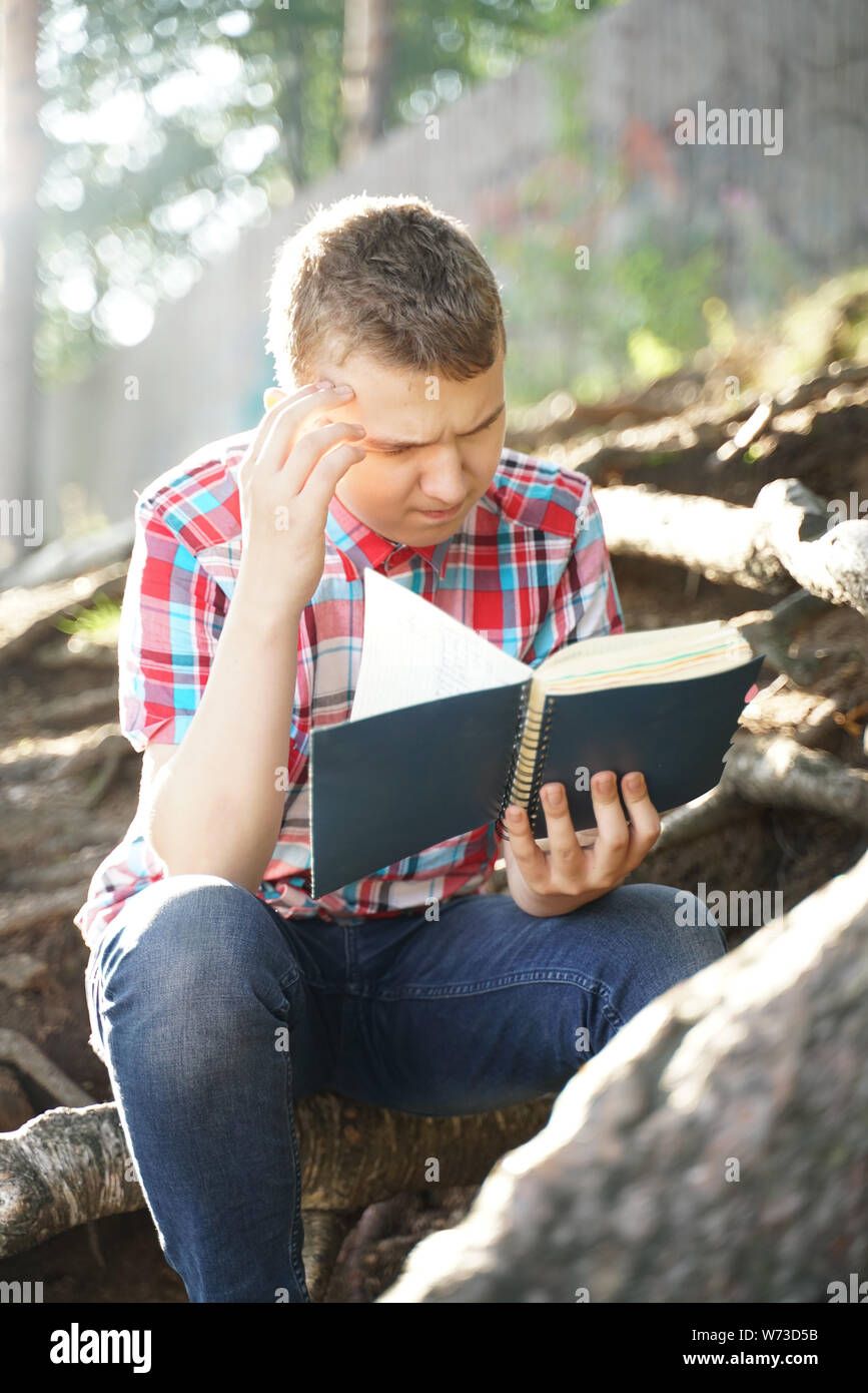 Teenage boy reading exercise book on the nature Stock Photo - Alamy