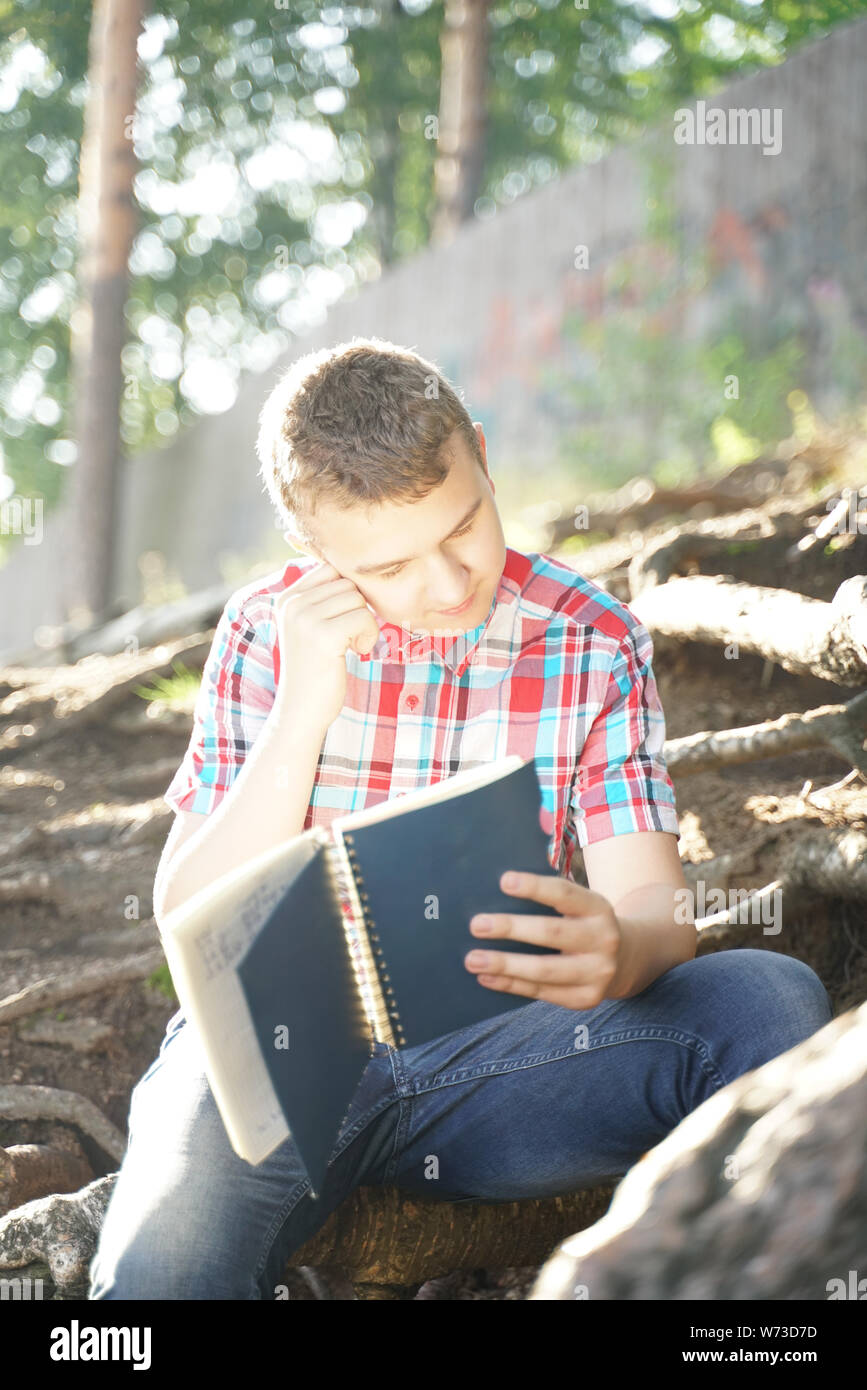 Teenage boy reading exercise book on the nature Stock Photo - Alamy