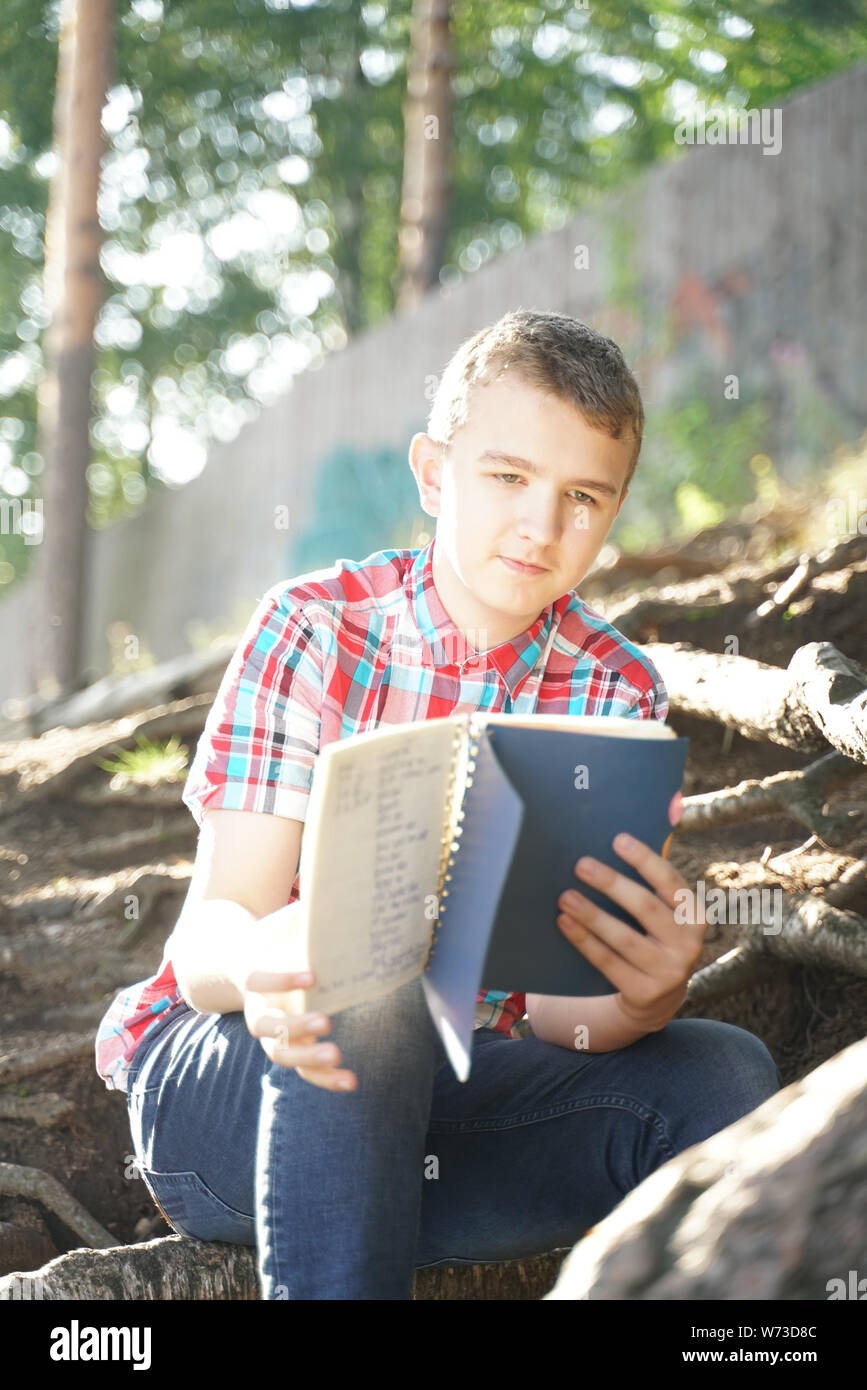 Teenage boy reading exercise book on the nature Stock Photo - Alamy