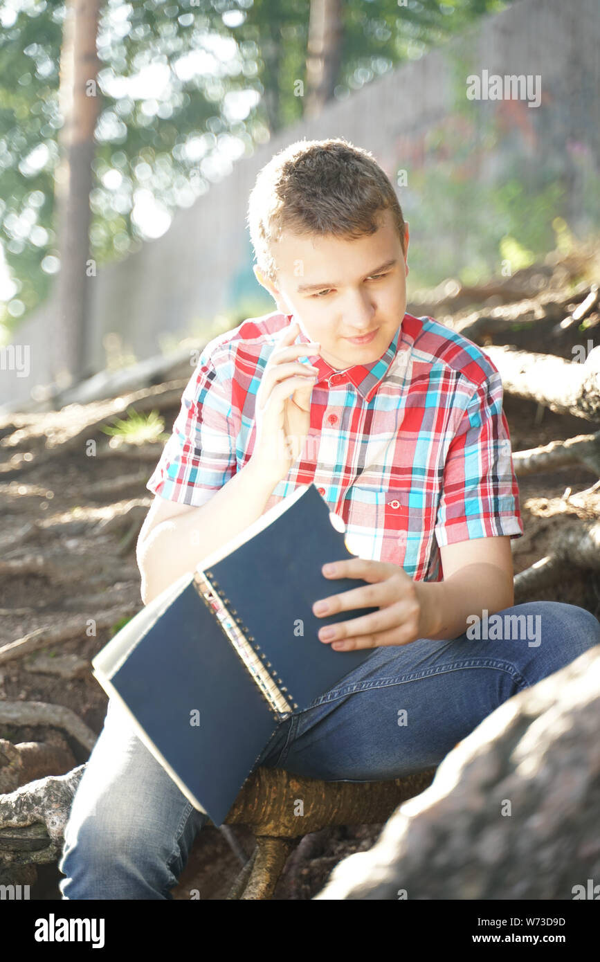 Teenage boy reading exercise book on the nature Stock Photo - Alamy