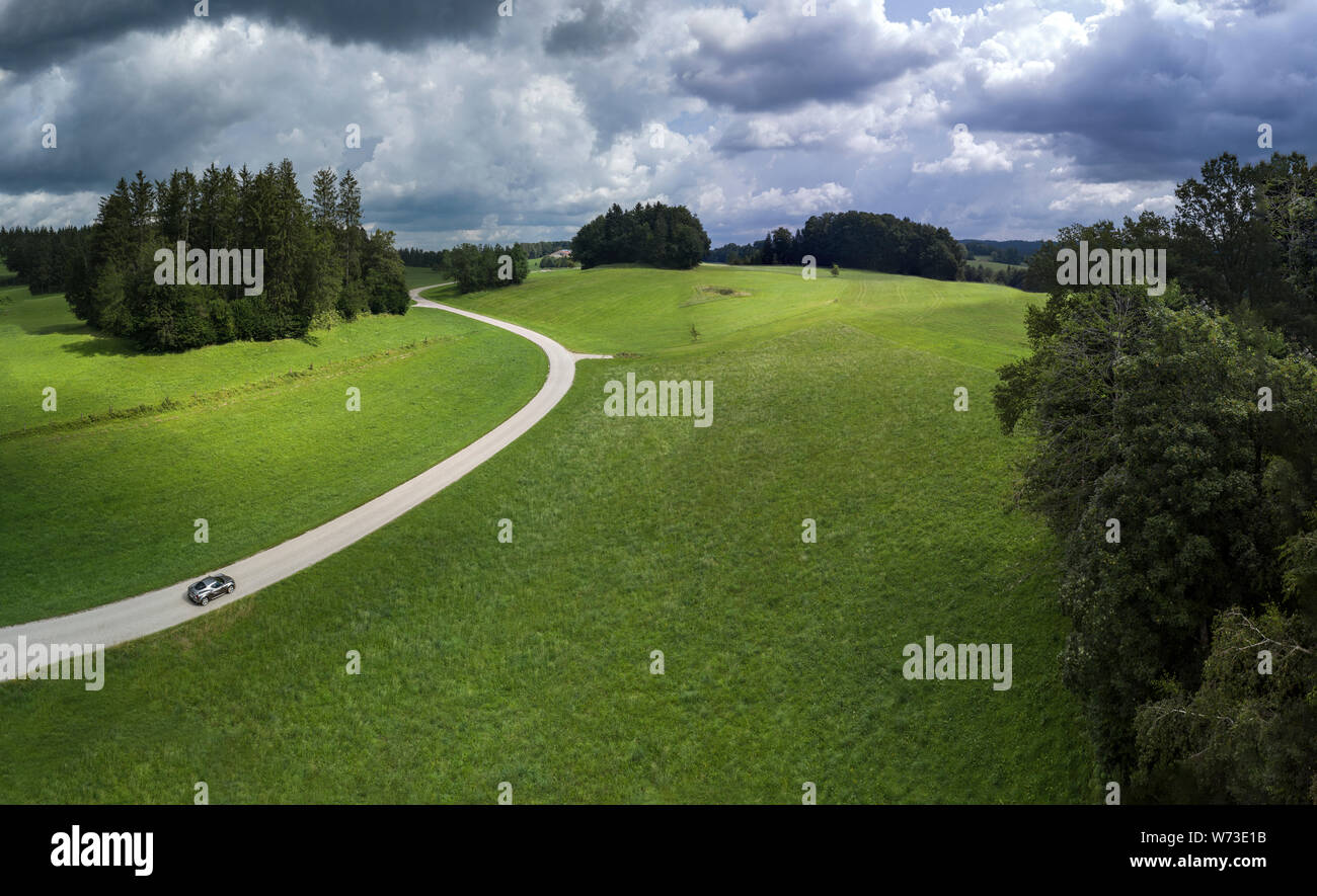 Aerial of car driving along countryside road through green fields in ...