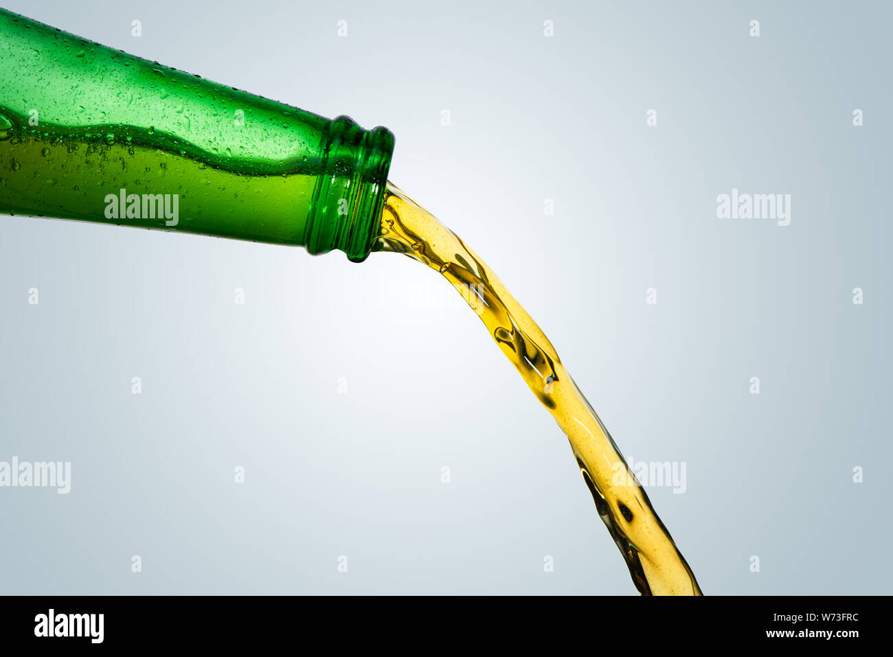 Refreshing ice cold beer pouring from neck of green bottle. Closeup on ...