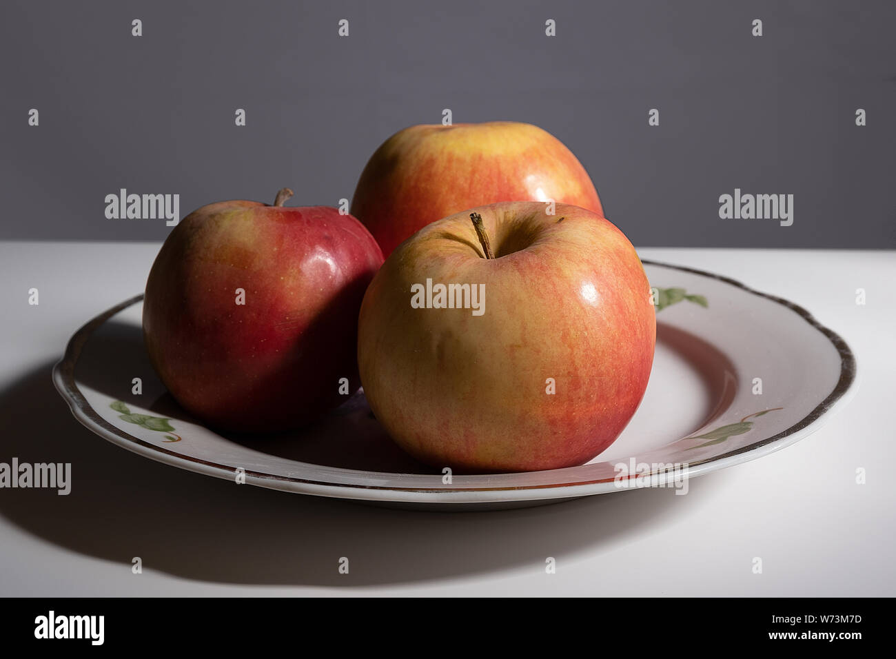 Three apples on a plate on a table in the kitchen. Low key Stock Photo ...