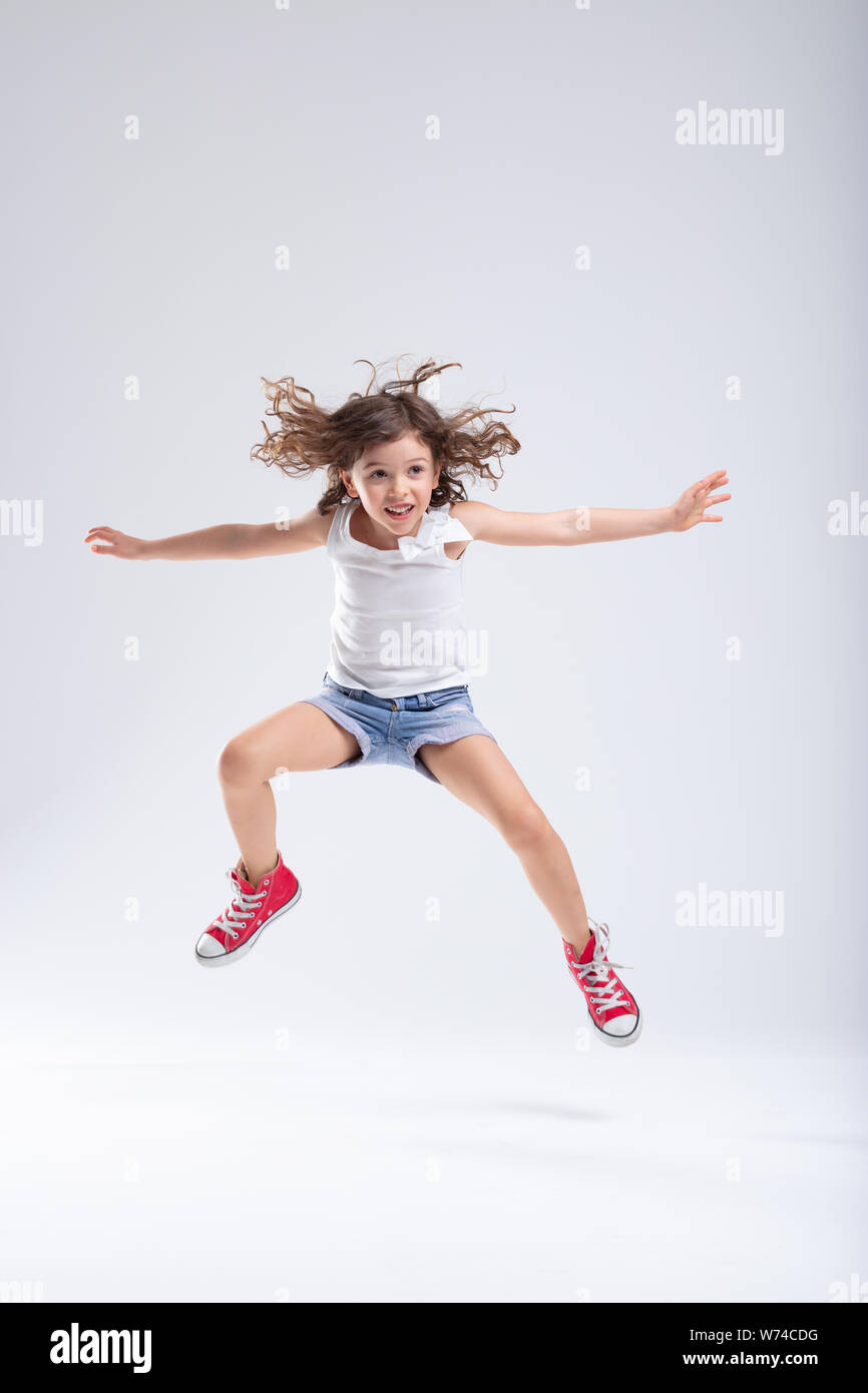 Hyperactive little girl leaping into the air with arms outstretched and ...