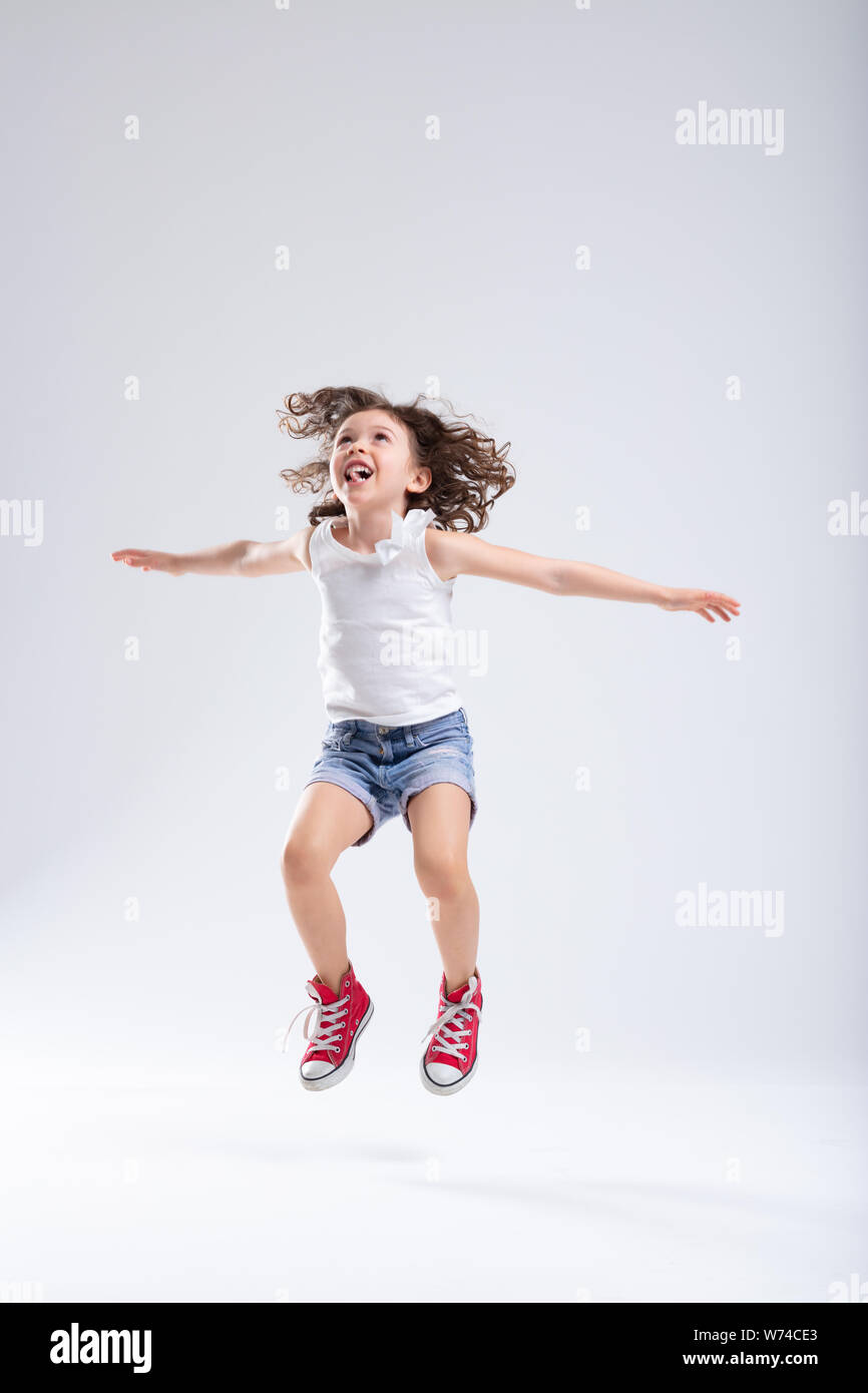 Joyful energetic active little girl in denim shorts and red sneakers ...