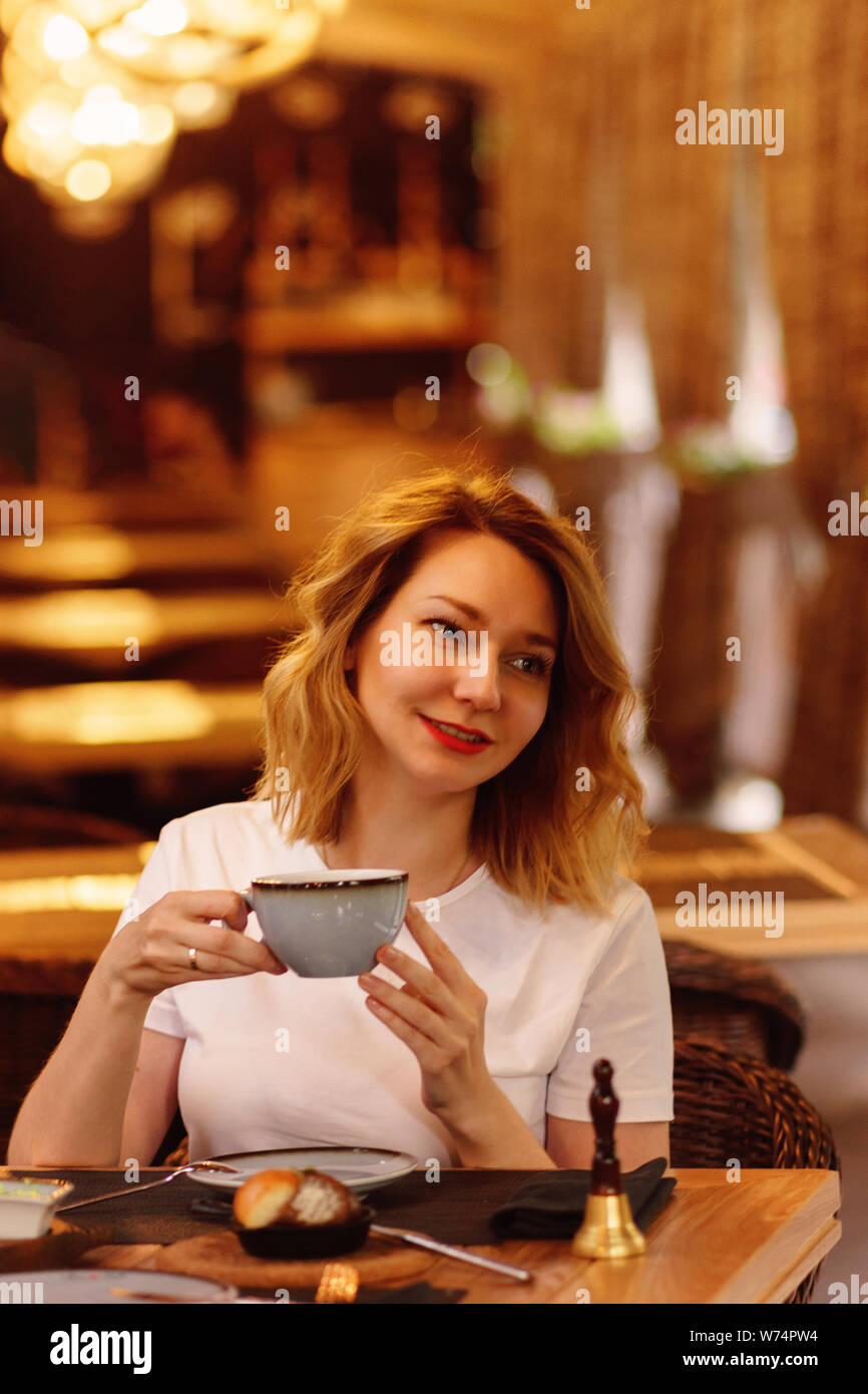 Pretty woman in a white t-shirt is drinking tea on a summer terrace of ...