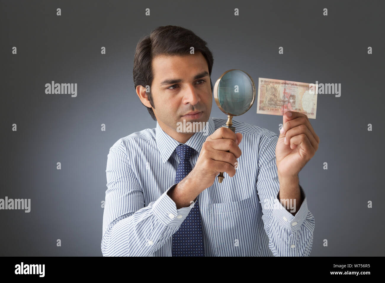Businessman examining one thousand rupee banknote with magnifying glass ...