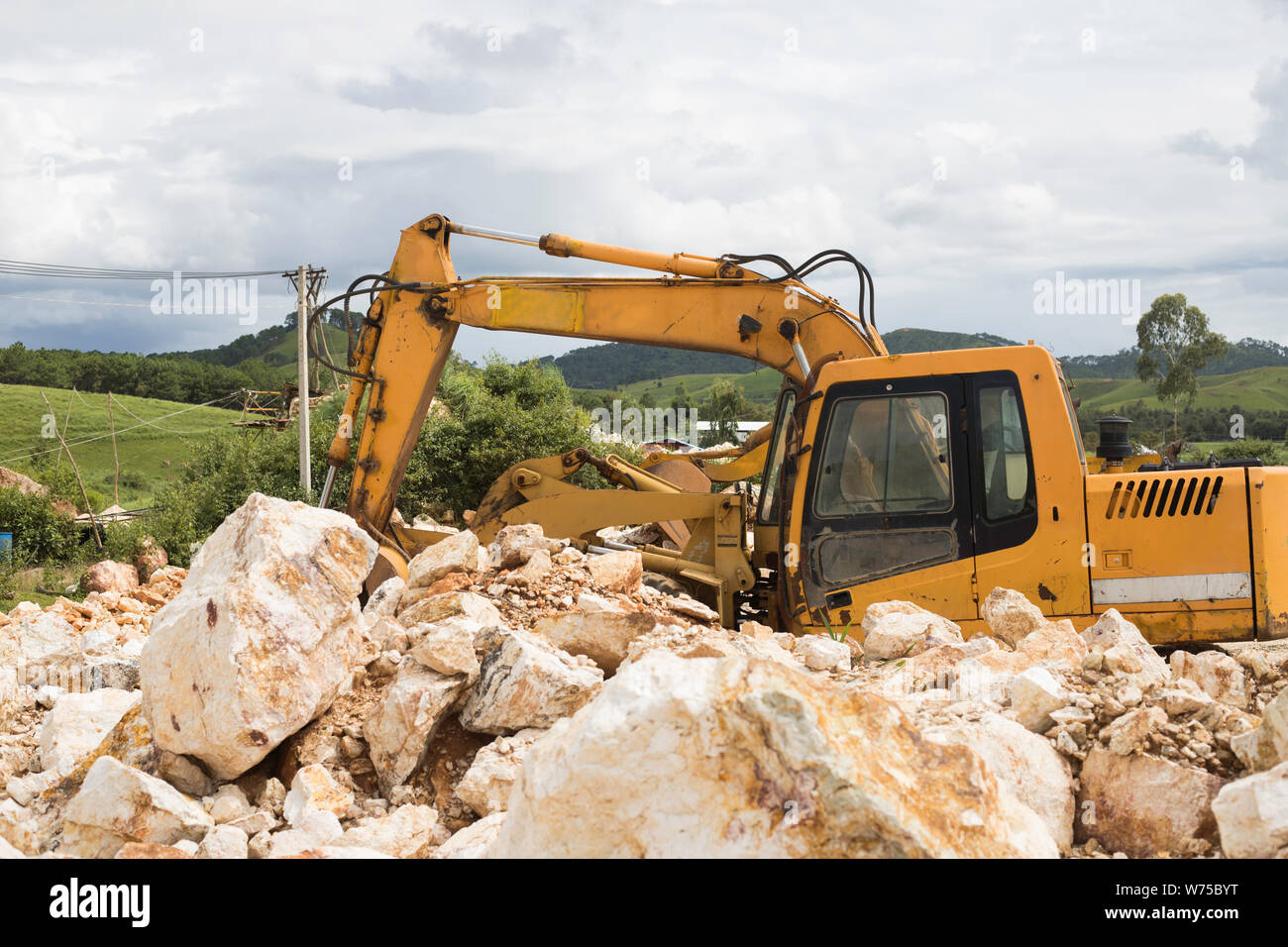 tractor working on big stones at mountains with grass and trees ...