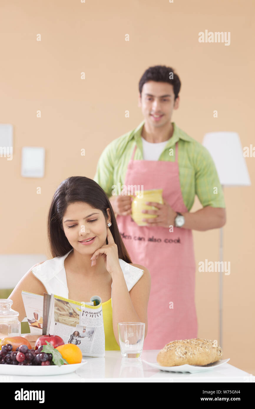 Woman reading a magazine with her husband serving jug Stock Photo - Alamy