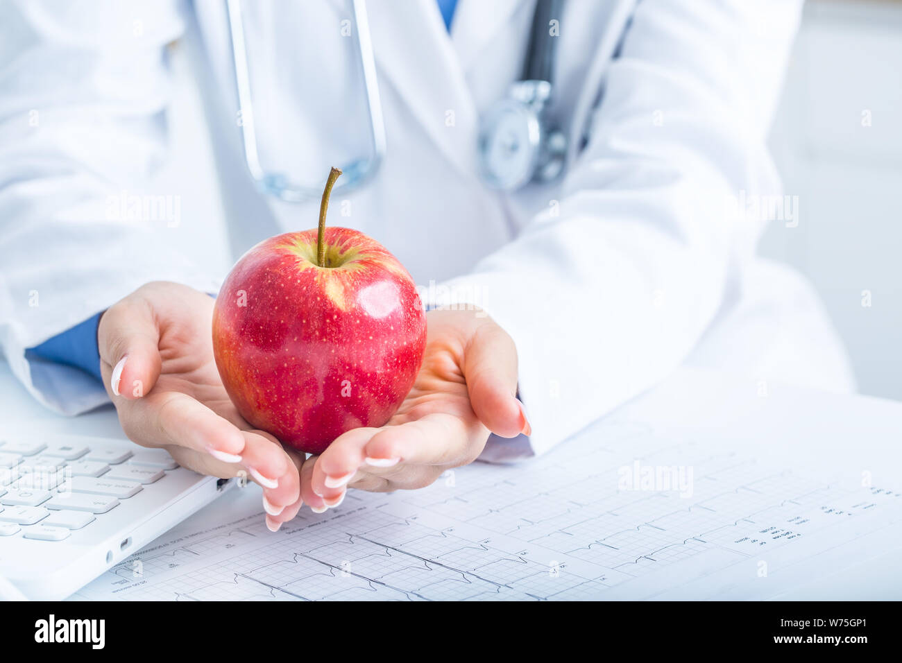 Woman doctor in ambulance holds red apple in hands. On desk laptop and ...