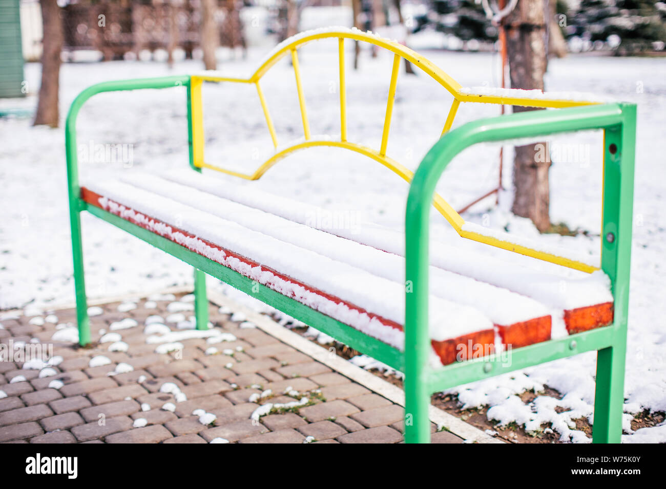 Multi-colored metal bench covered with the snow in a city park. Close ...