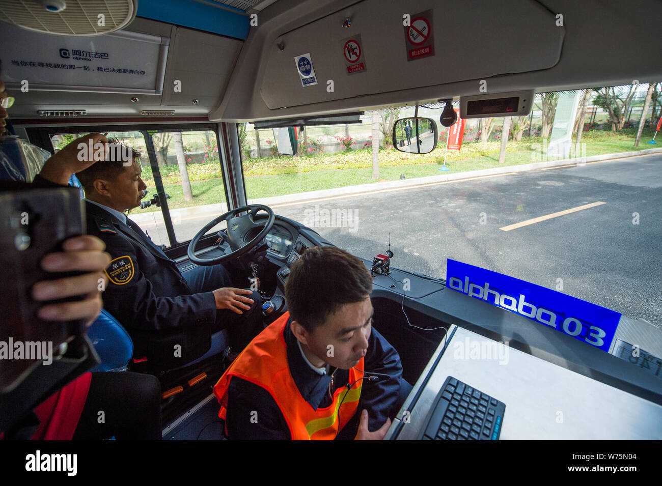 A driver sits in the driver's seat on a self-driving bus on a street ...