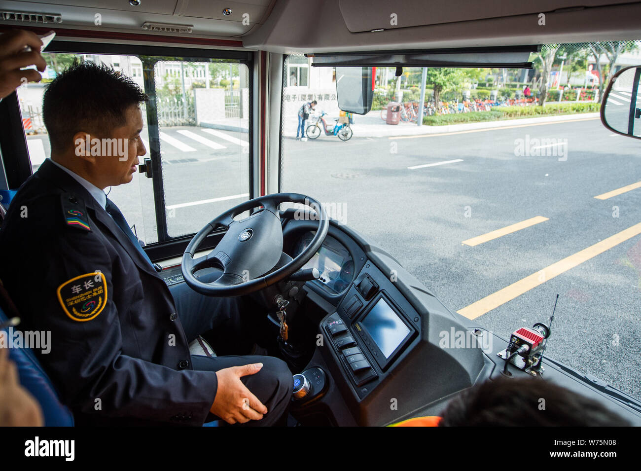 A driver sits in the driver's seat on a self-driving bus on a street ...