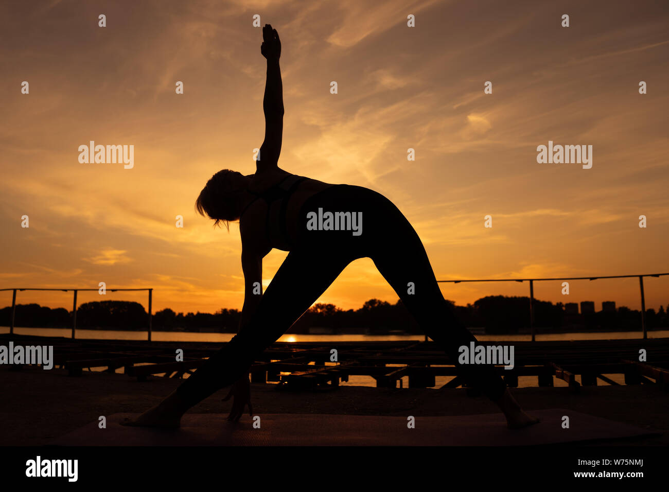 Woman practicing yoga in sunset. Trikonasana, Bikram triangle left ...