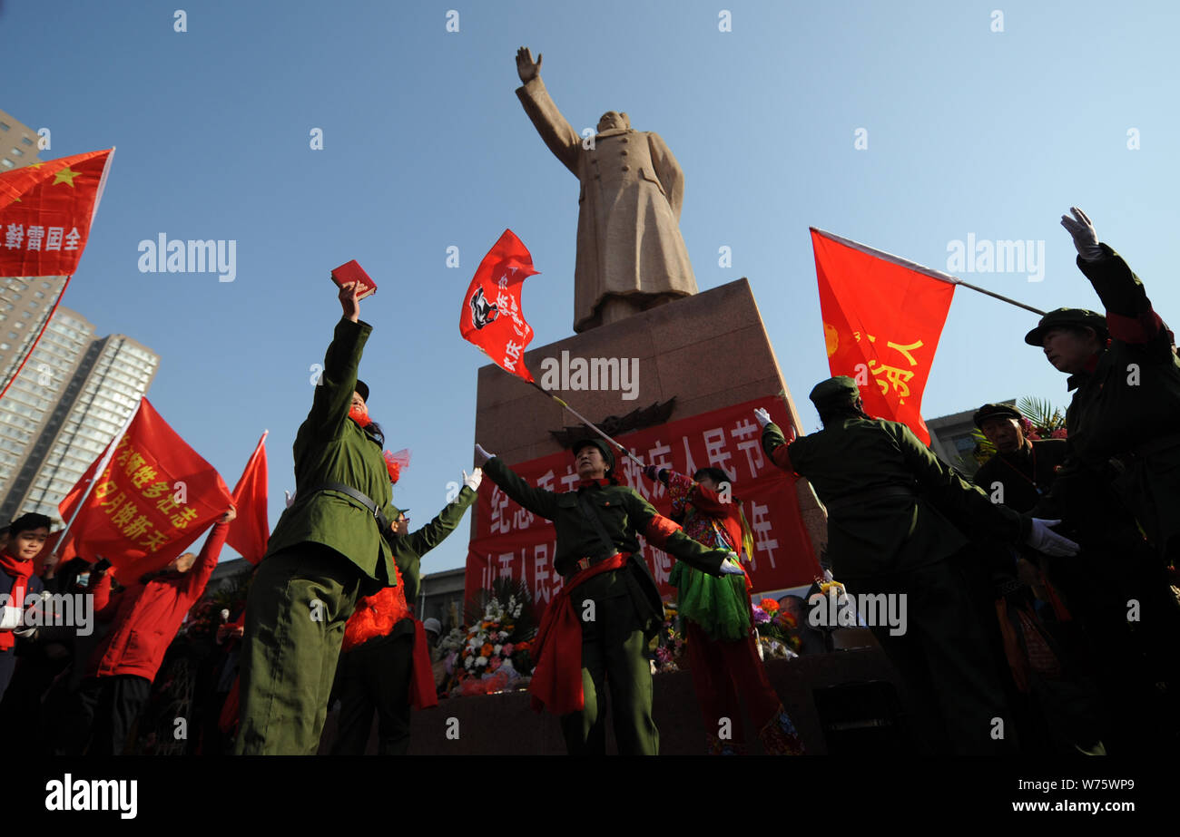 Chinese people in uniform wave red flags in front of a statue of ...