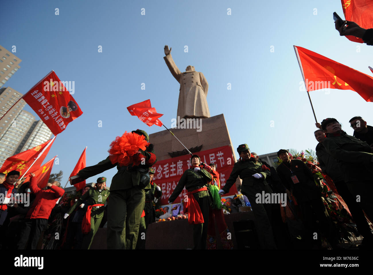 Chinese people in uniform wave red flags in front of a statue of ...