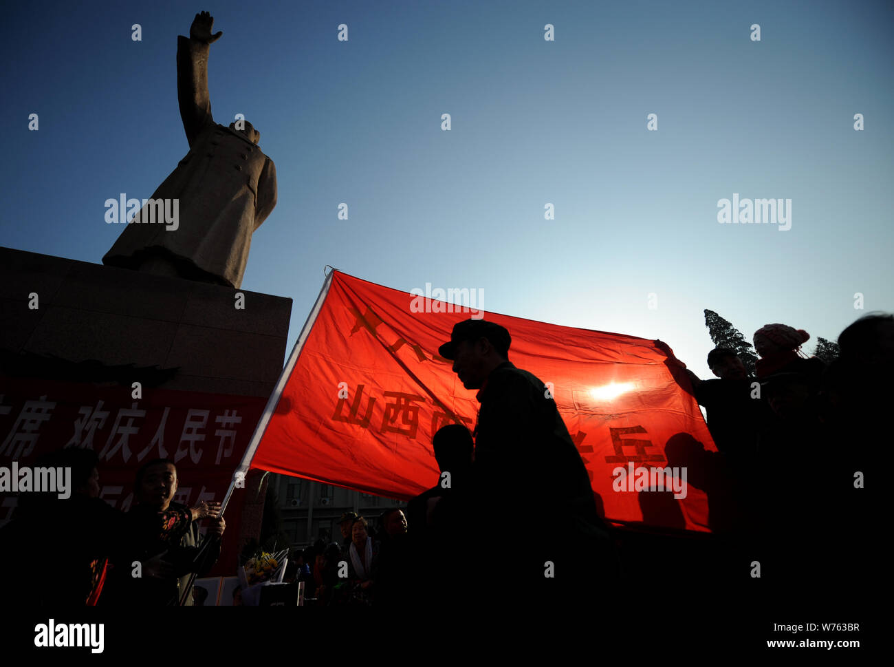 Chinese people in uniform wave red flags in front of a statue of ...
