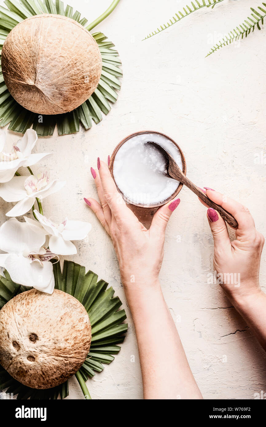 Female hands holding bowl and spoonful of coconut oil light background ...