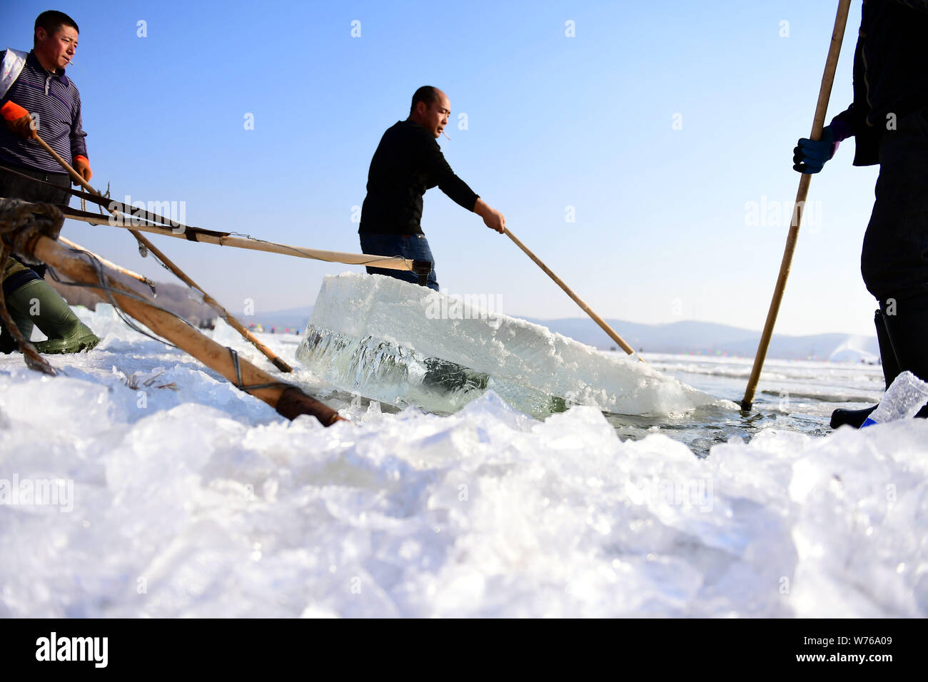 Chinese workers drag an ice block as others chisel it on the frozen ...