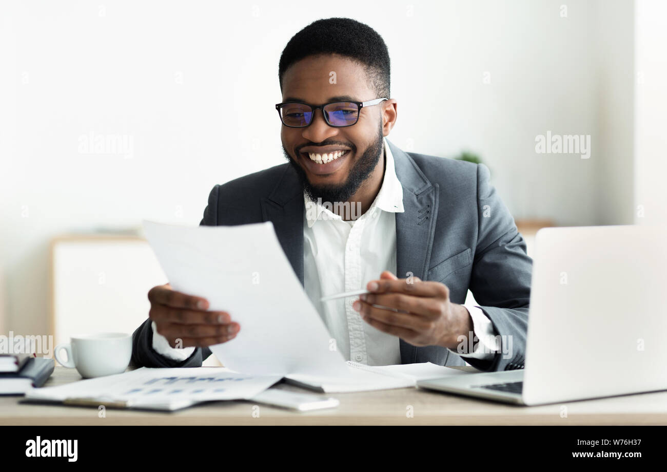 Smiling black businessman checking reports in modern office Stock Photo ...