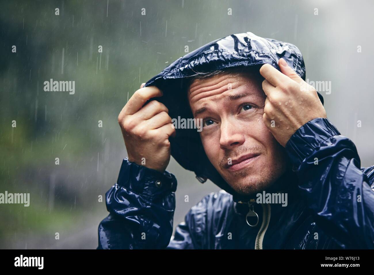 Trip in bad weather. Portrait of young man in drenched jacket in heavy ...