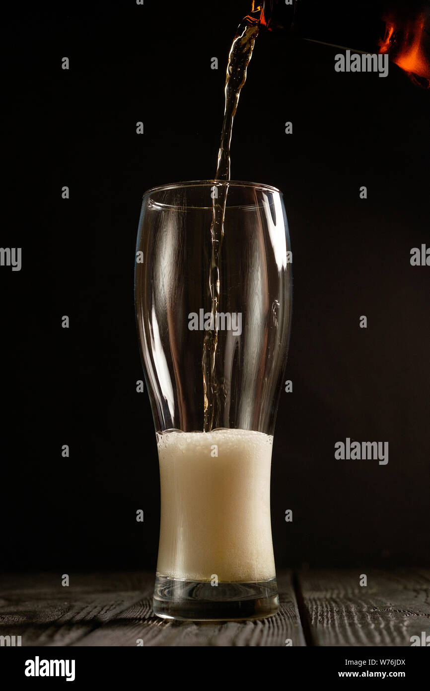 beer pours into glass on black background Stock Photo - Alamy