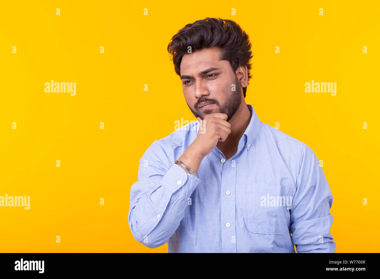 Apathetic cute young indian man is posing on a yellow background with ...