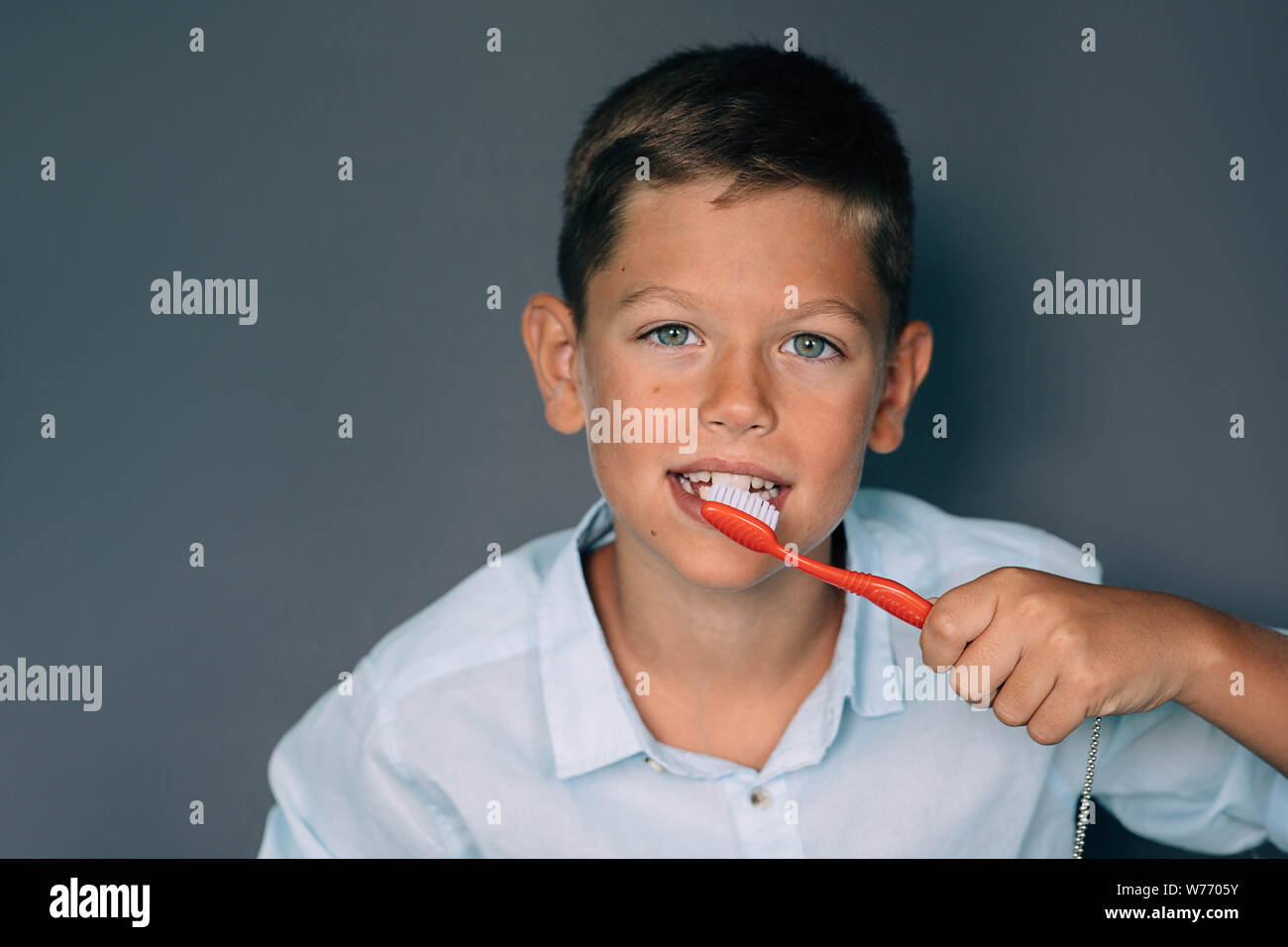 Cute boy brushing his teeth on gray background. Keeping teeth healthy ...
